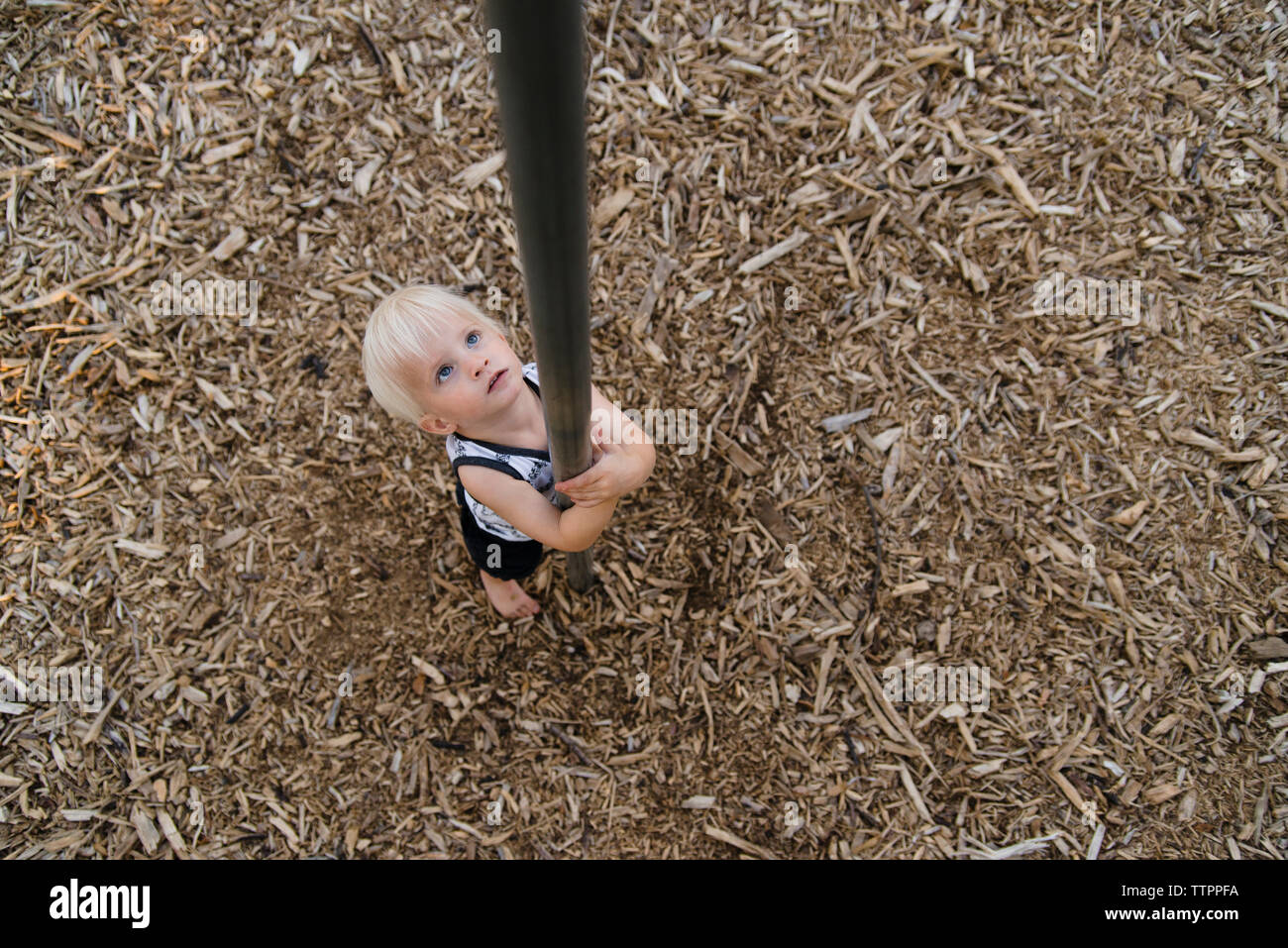 High angle view of baby boy looking up while standing by pole on field ...