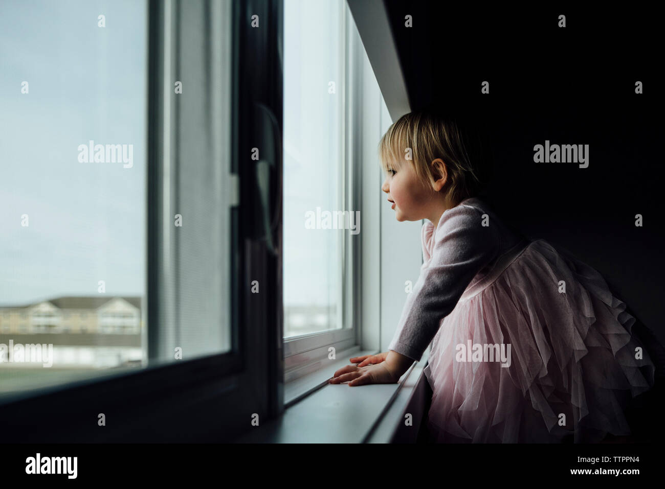 Side view of girl standing by window at home Stock Photo - Alamy