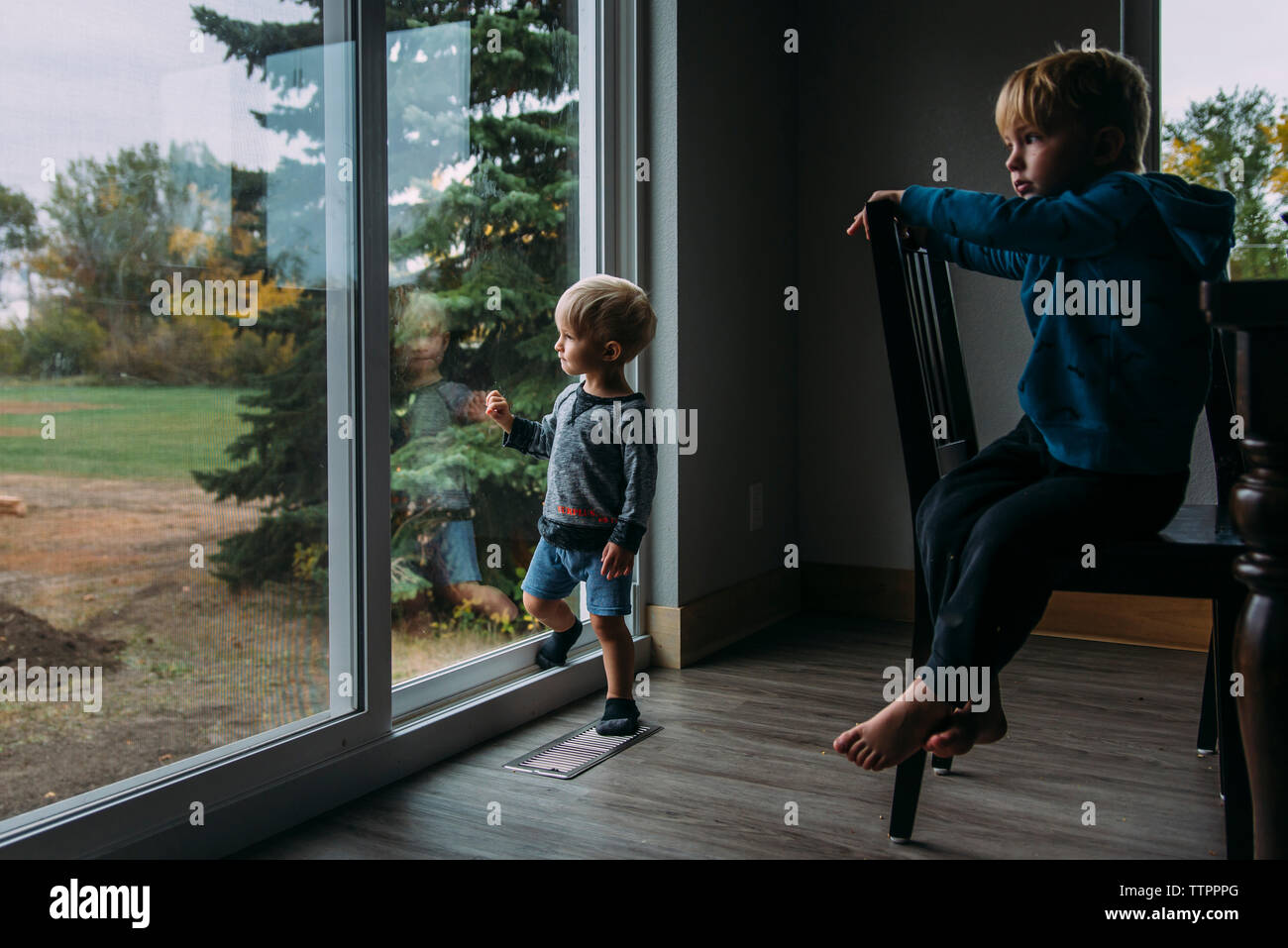 Thoughtful brothers looking through window at home Stock Photo - Alamy