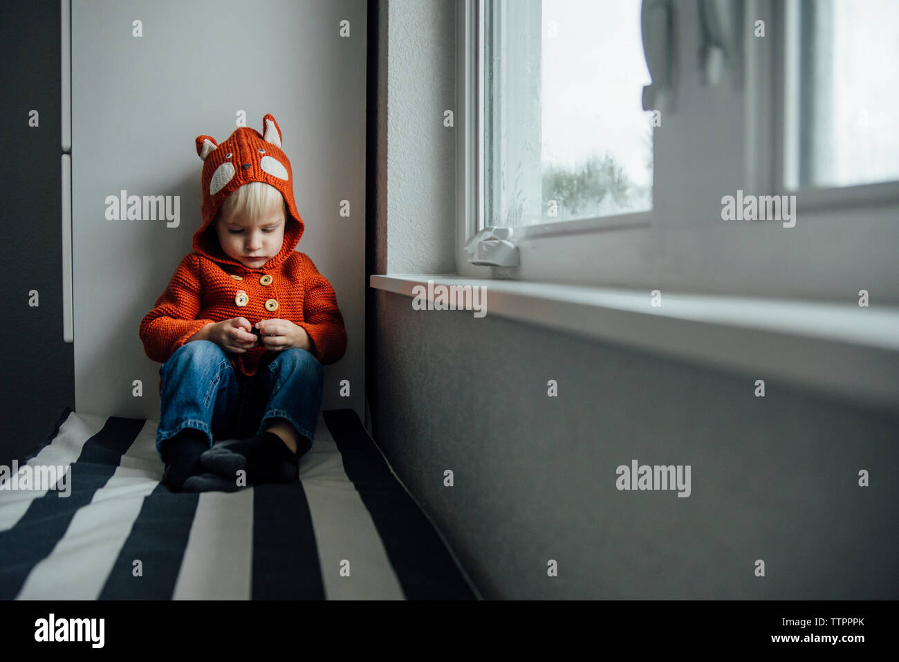 Cute boy wearing warm clothing while sitting by window at home Stock ...