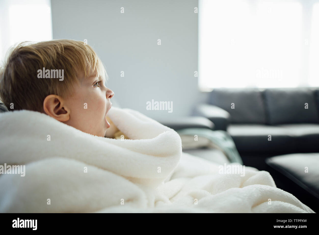 Side view of boy yawning while sitting on sofa at home Stock Photo - Alamy