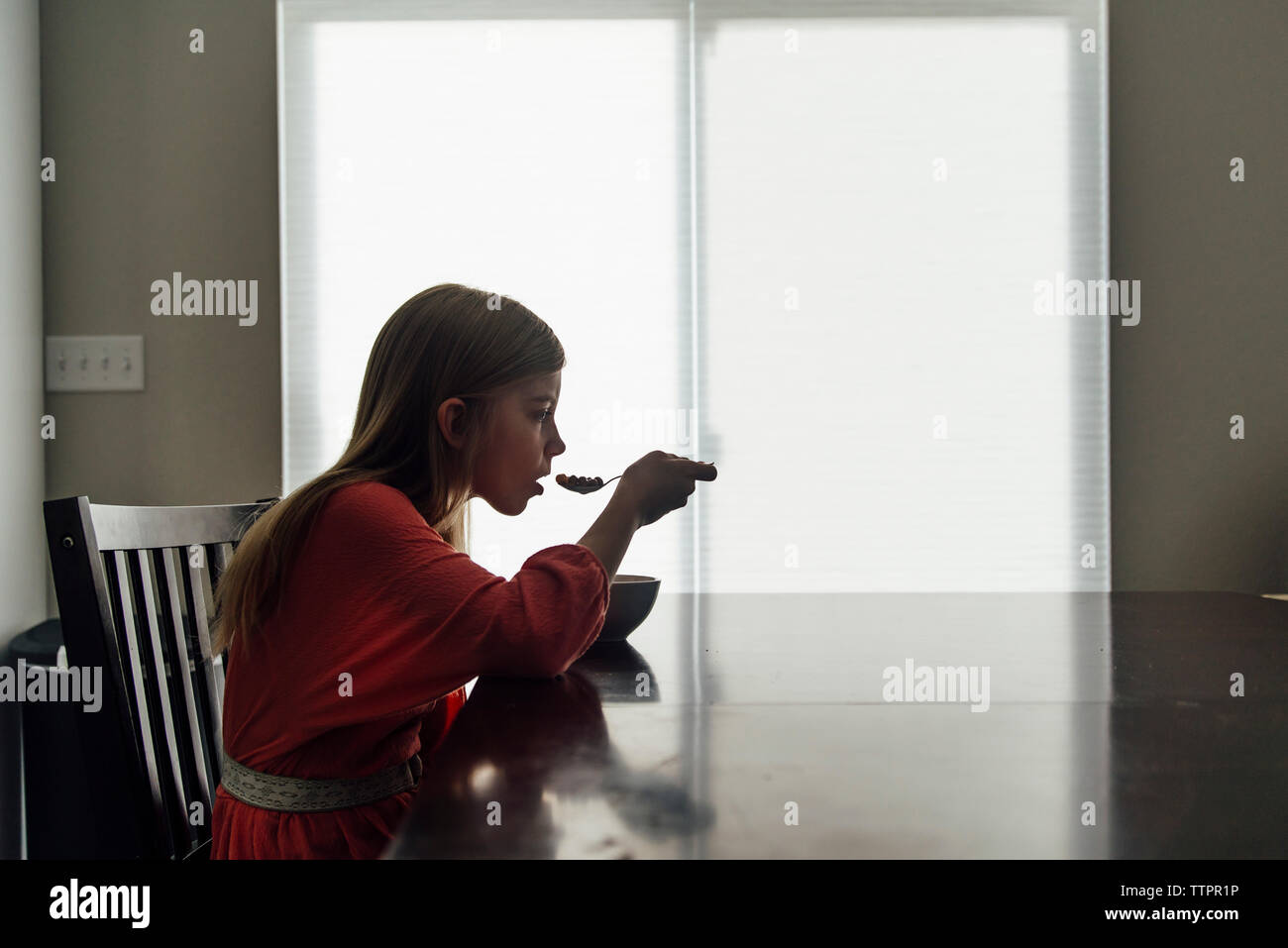 Side view of girl eating food while sitting at home Stock Photo - Alamy