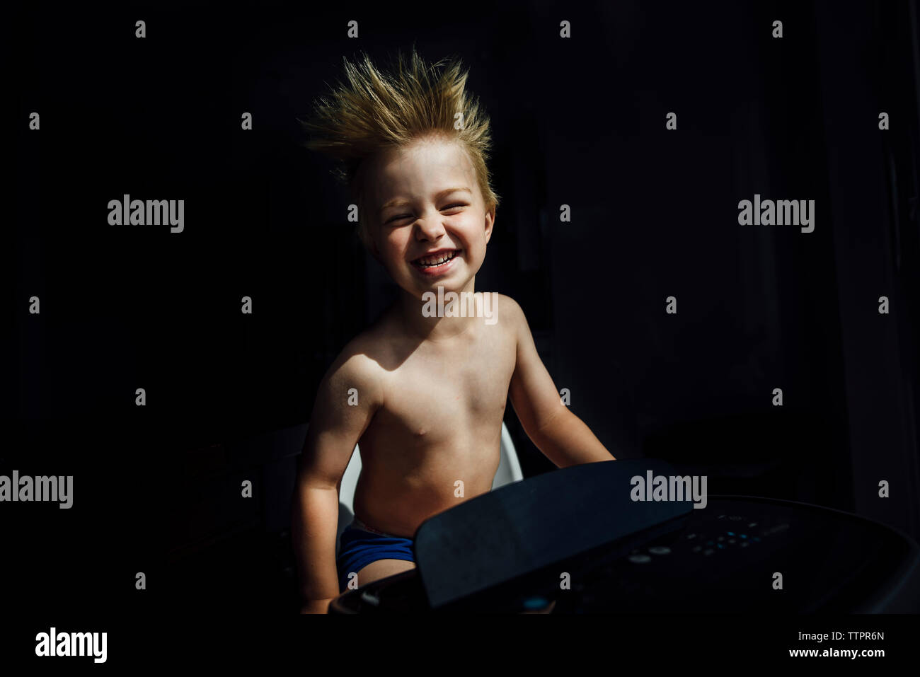 Portrait of happy shirtless boy enjoying breeze from air conditioner in ...