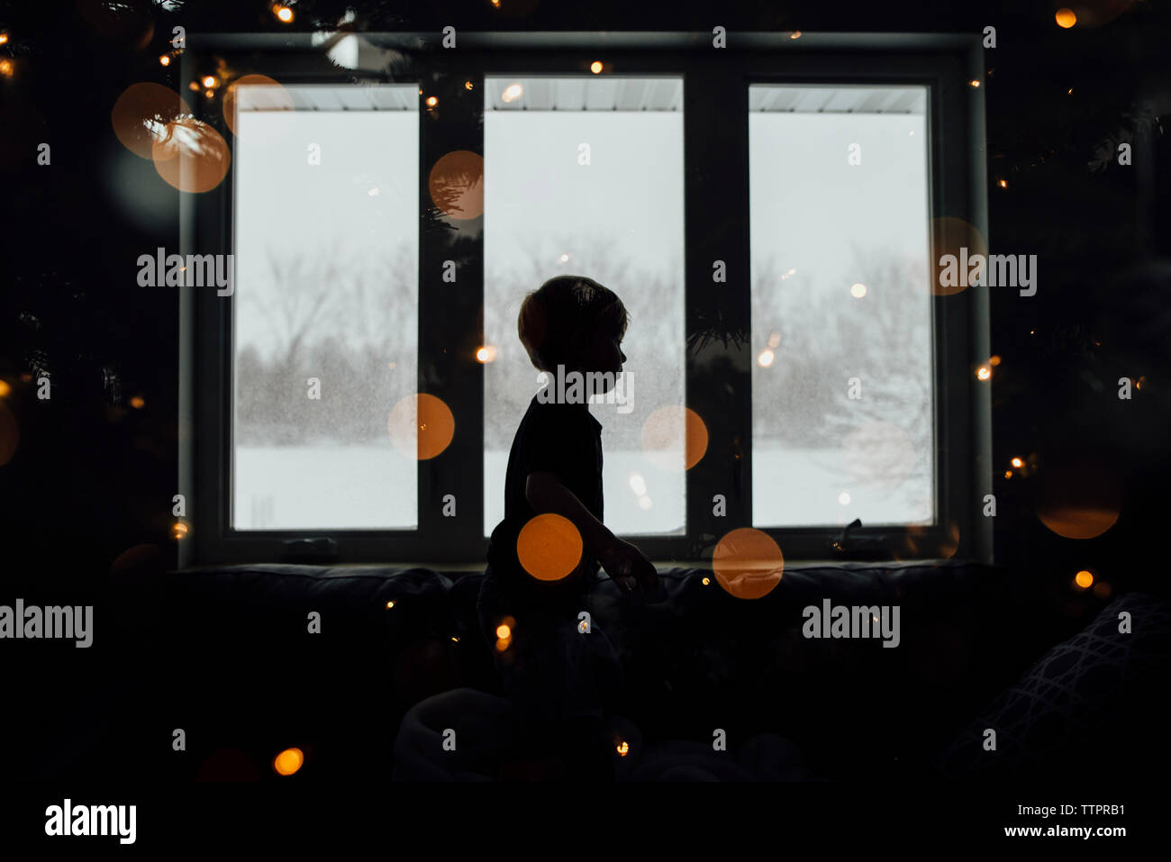 Side view of silhouette boy standing by window in illuminated room at ...