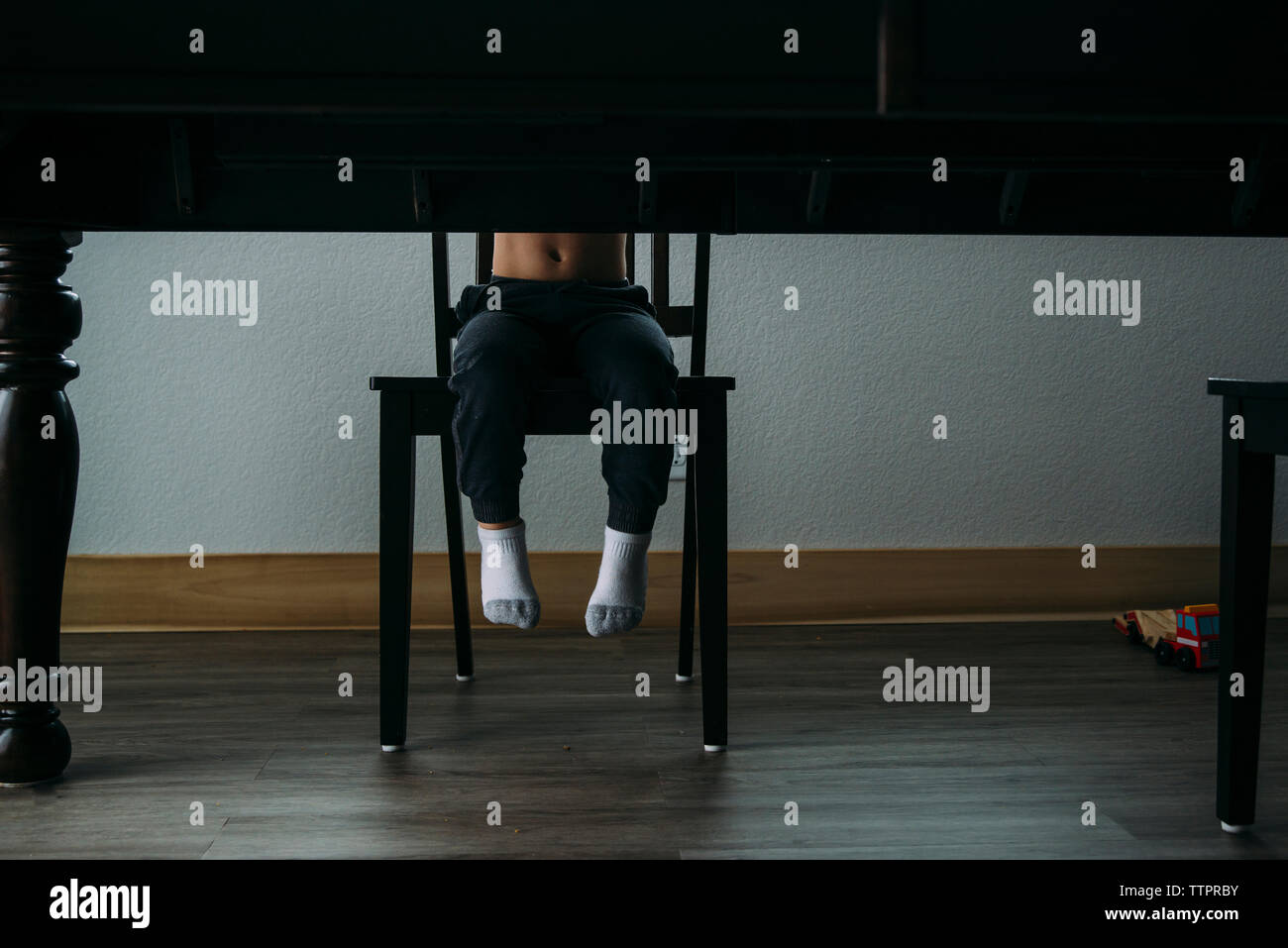 Low section of boy sitting on chair by table at home Stock Photo - Alamy
