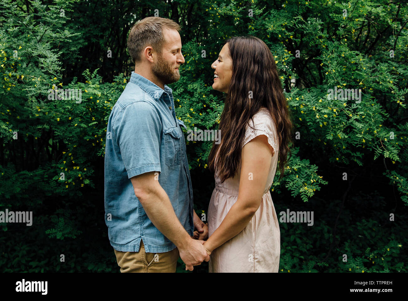 Side view of smiling couple standing against plants Stock Photo - Alamy