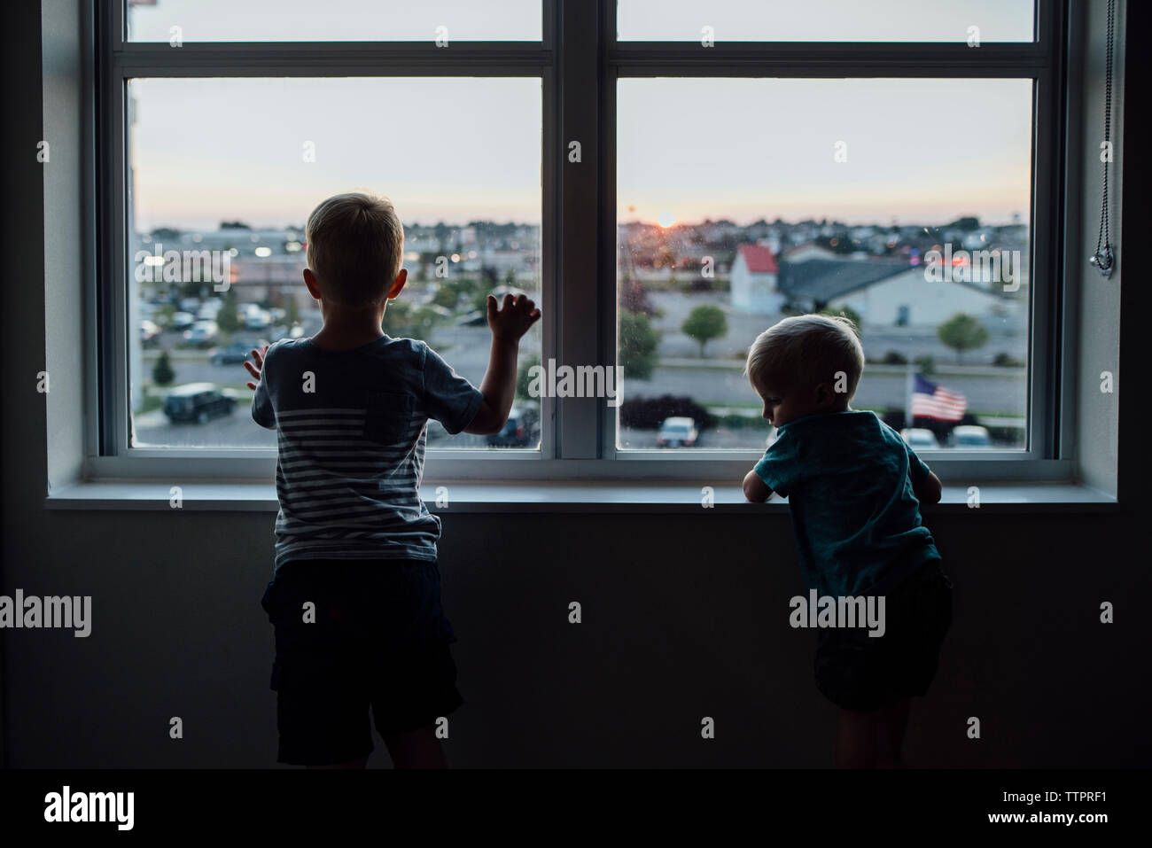 Rear view of brothers looking through window while standing at home ...
