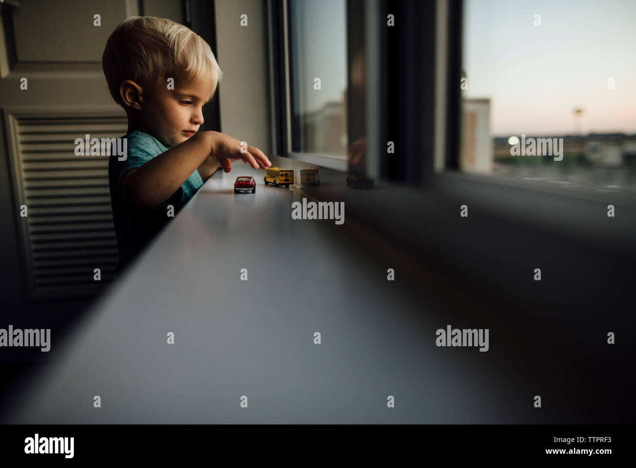 Side view of baby boy playing with toy cars on window sill at home ...
