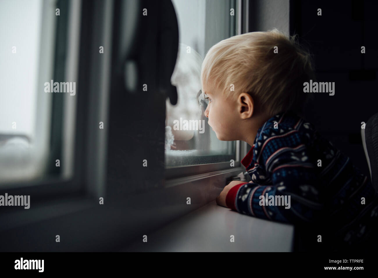 Side view of baby boy looking through window while standing at home ...