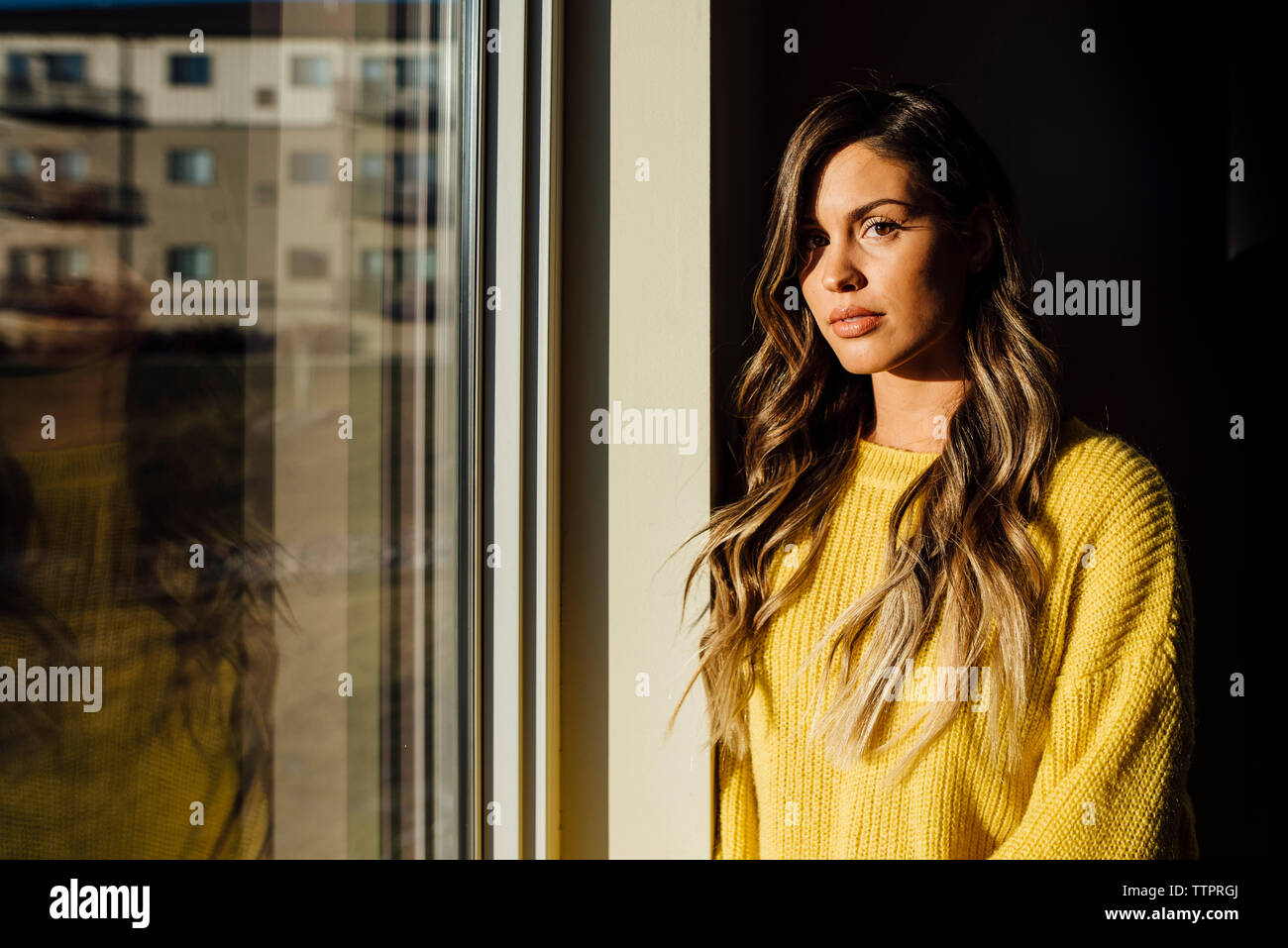 Portrait of woman standing by window at home Stock Photo - Alamy