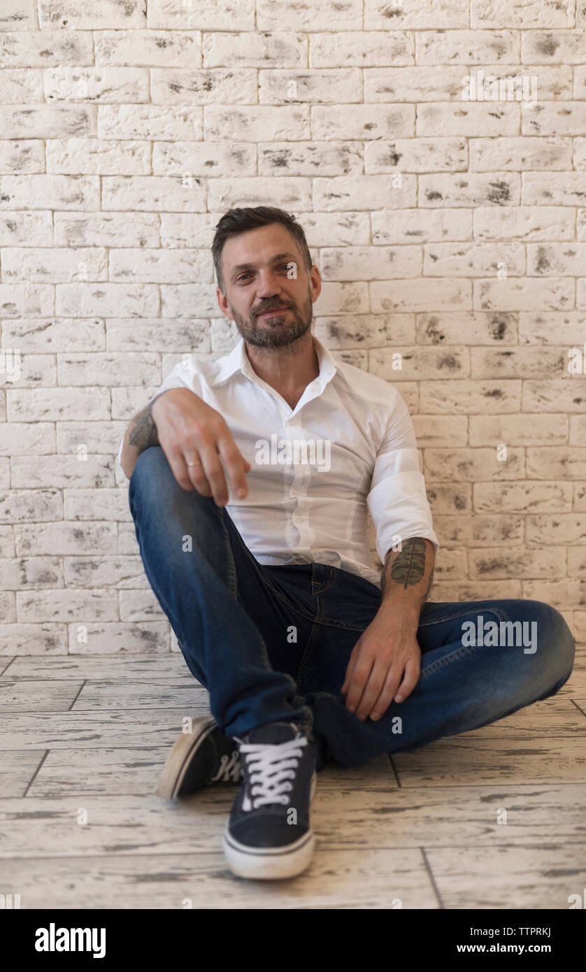 Portrait of confident man with hand on knee sitting against wall Stock ...