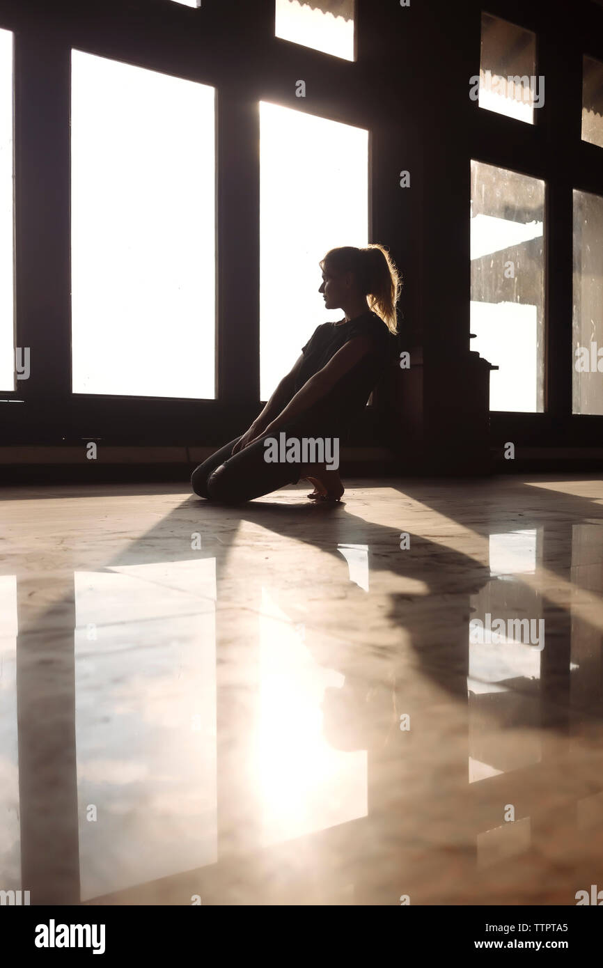 Full length of thoughtful young woman kneeling on tiled floor while ...