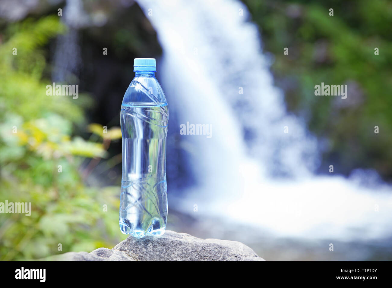 Bottle of clear water on blurred waterfall background Stock Photo - Alamy