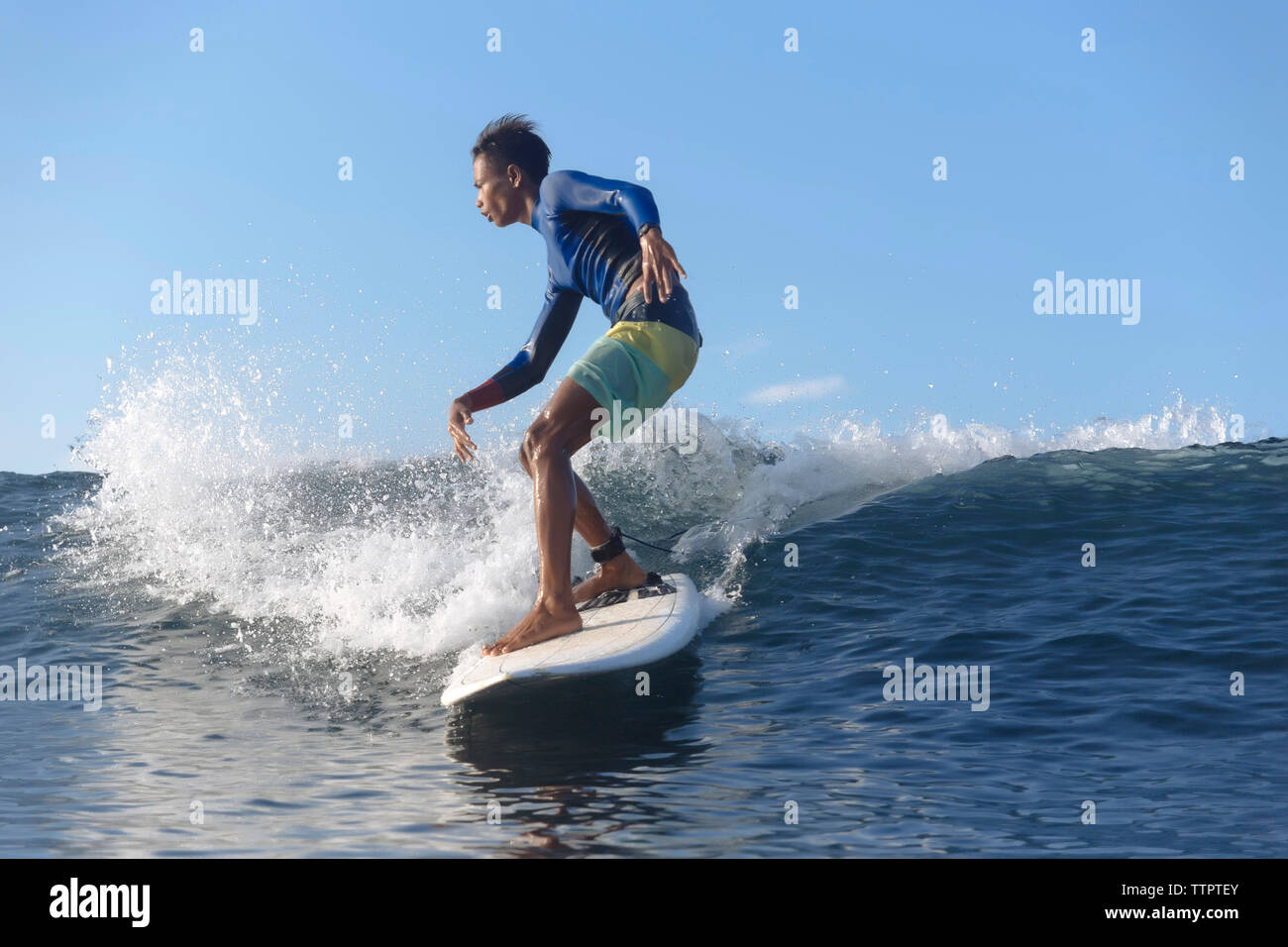 Side view of boy surfing on sea against blue sky Stock Photo - Alamy