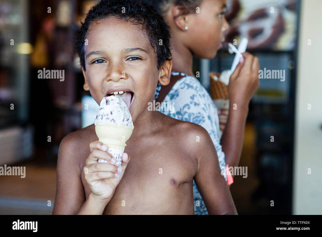 Portrait Of Shirtless Brother Licking Ice Cream While Standing By