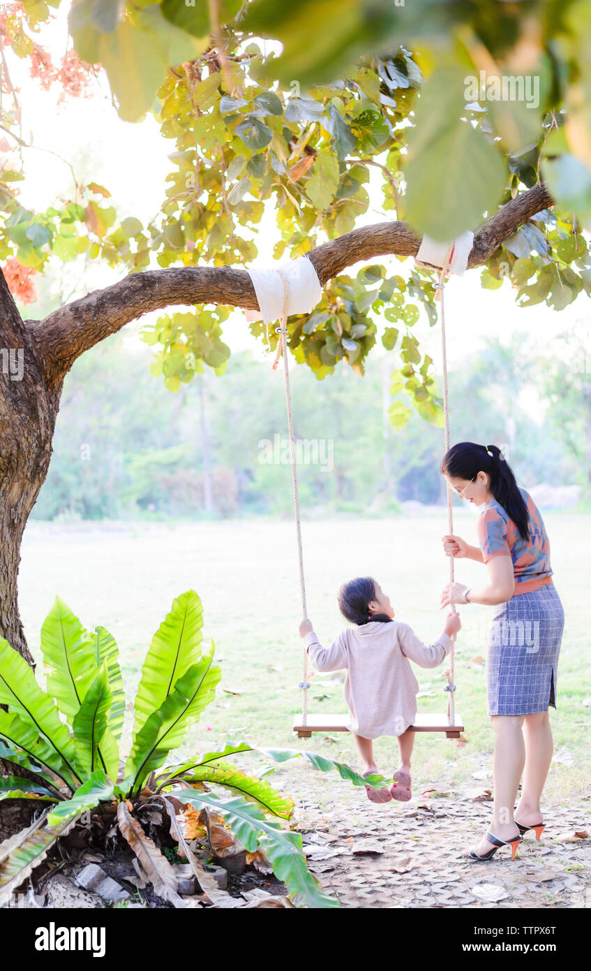 Mother swinging daughter on rope swing at park Stock Photo - Alamy
