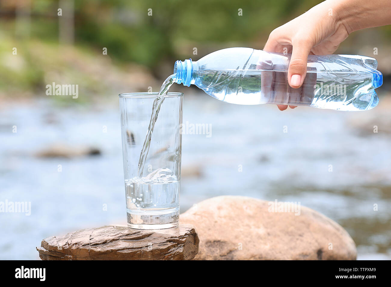 Water pouring in glass on blurred river background Stock Photo - Alamy