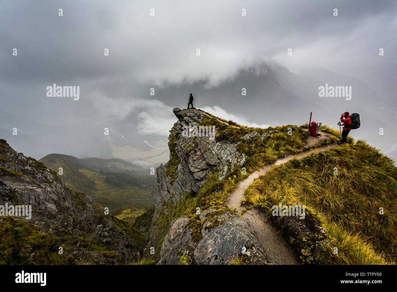 Figures overlooking a mountain valley hidden by clouds in New Zealand ...