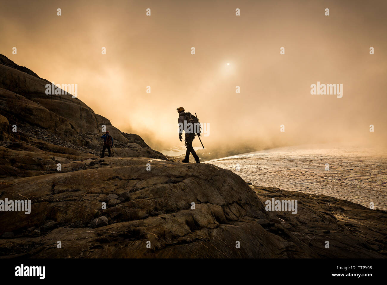 Two climbers walking across rocks above a glacier in New Zealand Stock ...