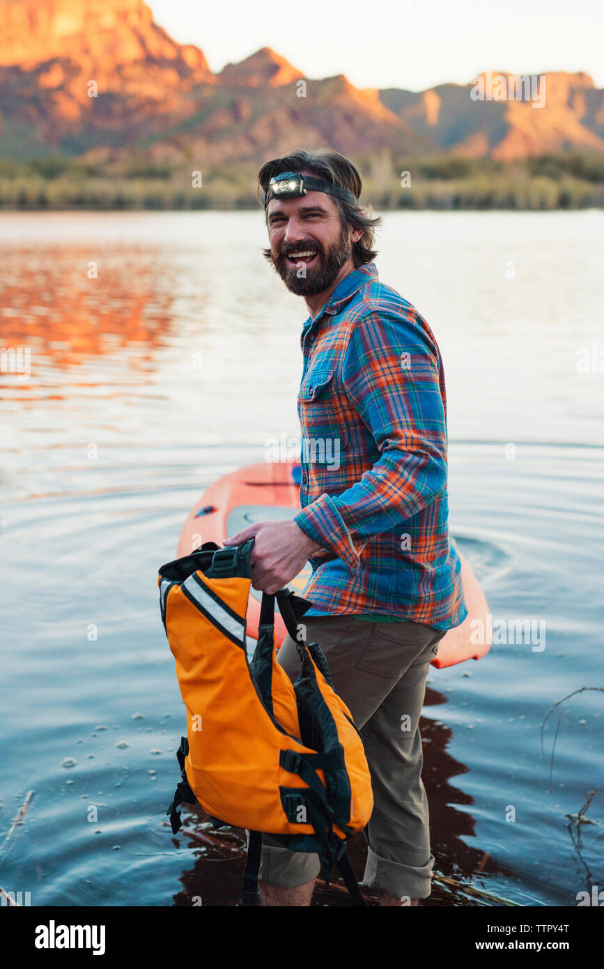 Side view portrait of happy man standing with paddleboard at lakeshore ...