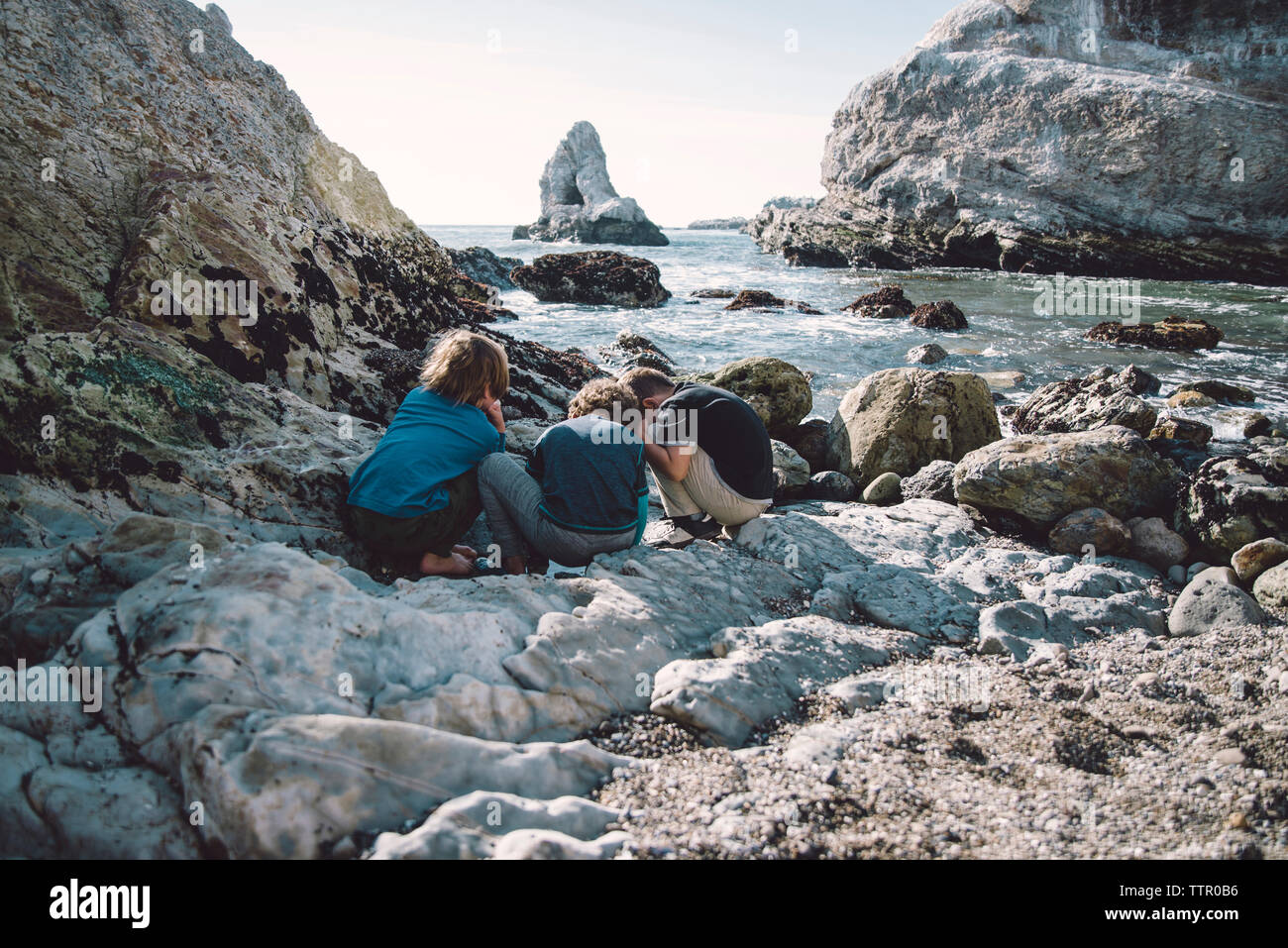 Friends playing while crouching on rocks at beach Stock Photo - Alamy