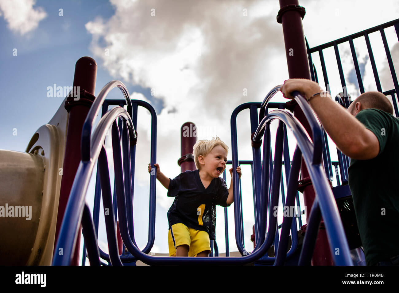 Low angle view of boy screaming to father while standing on slide in ...