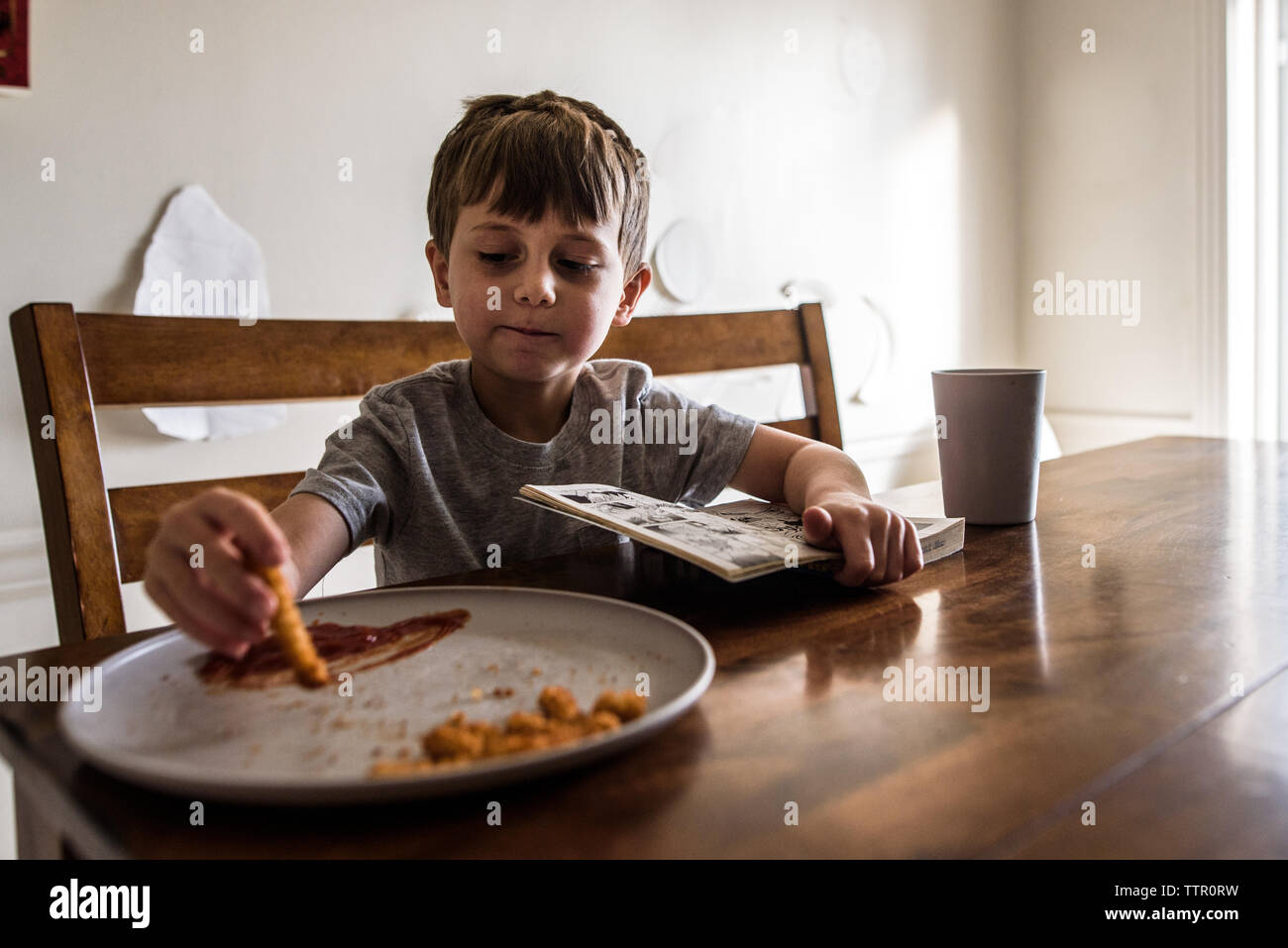 boy sitting at a table with book while eating french fries Stock Photo ...