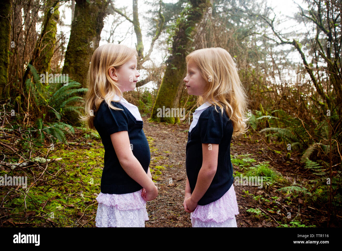 Twin girls standing on field against trees Stock Photo - Alamy
