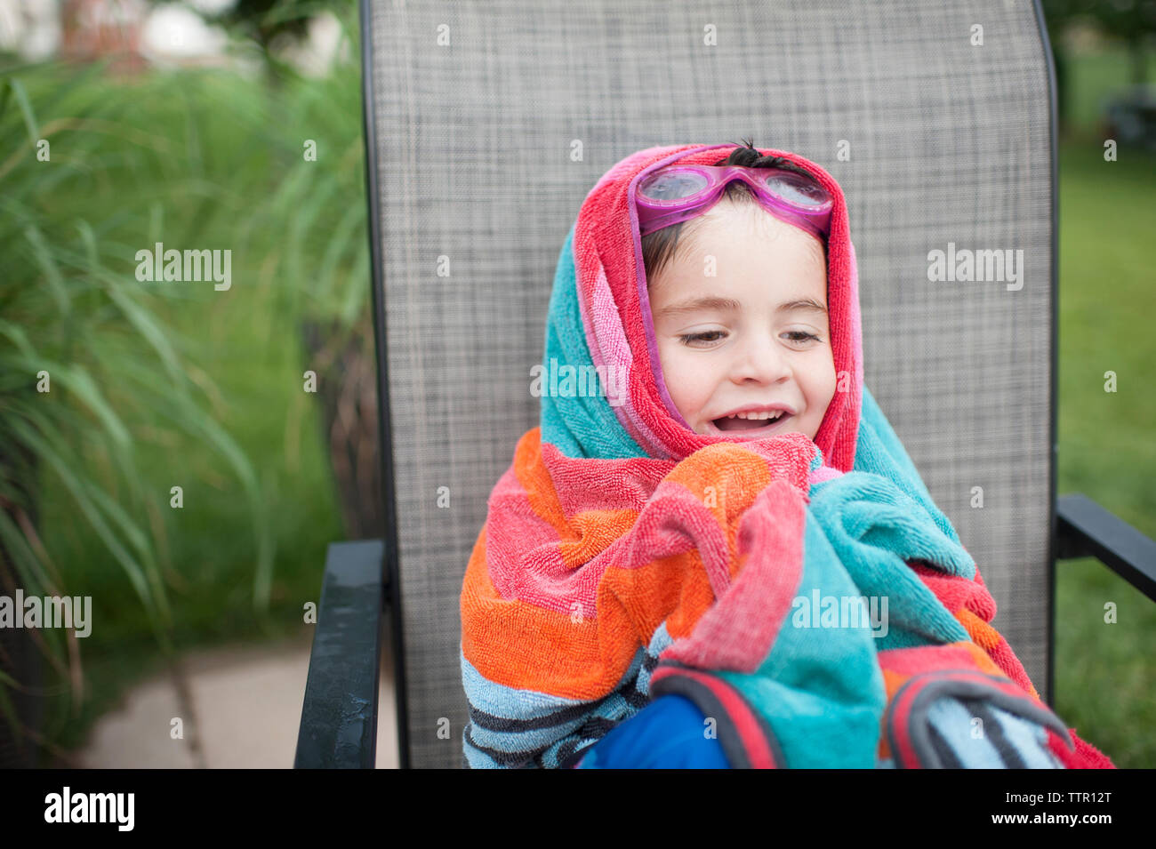 Boy wrapped in towel sitting on chair at backyard Stock Photo - Alamy
