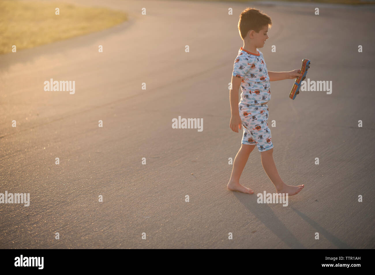 Side view of boy holding toy train while walking on road during sunset ...