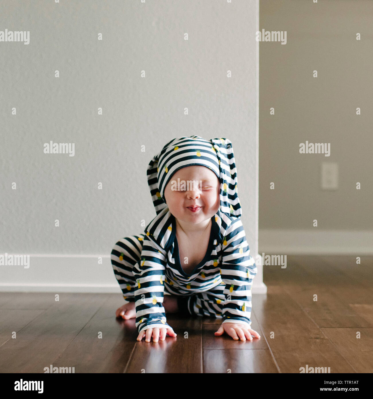 Cute playful baby boy making face while sitting on floor against wall ...