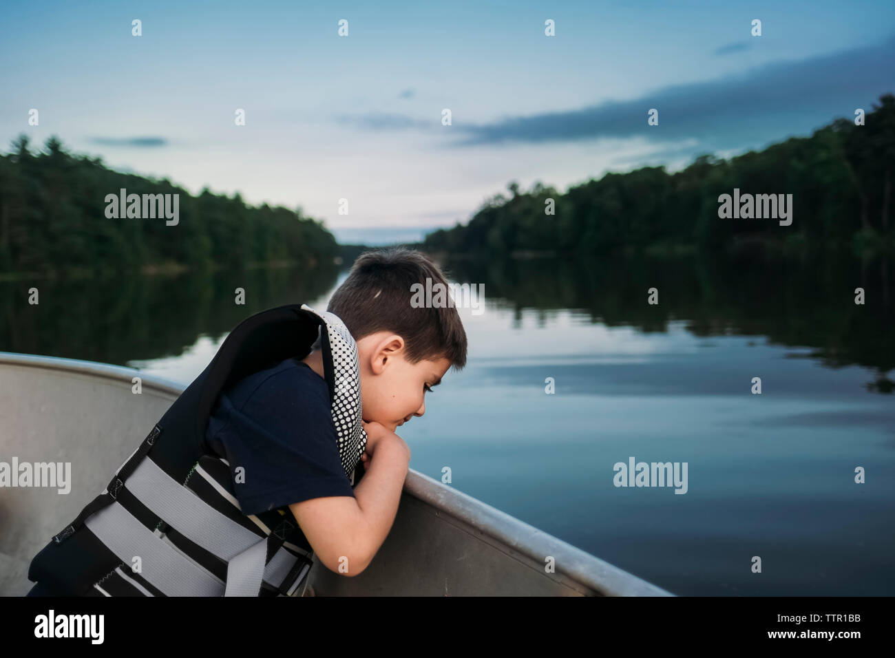 Side view of boy wearing life jacket while sitting in boat on lake ...