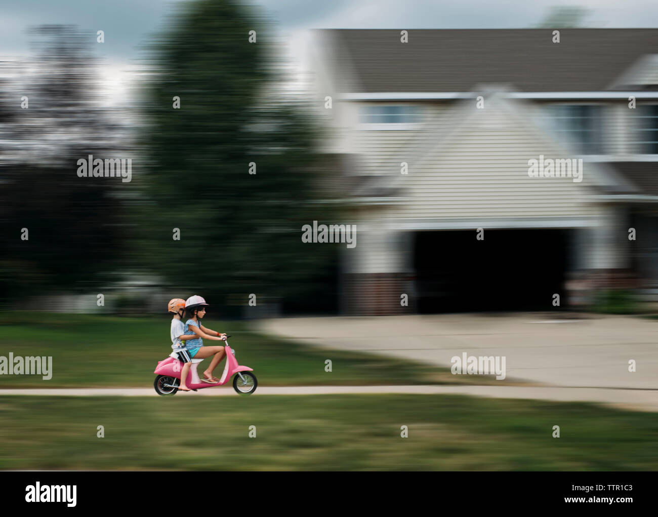 Side view of siblings riding moped scooter at driveway Stock Photo - Alamy