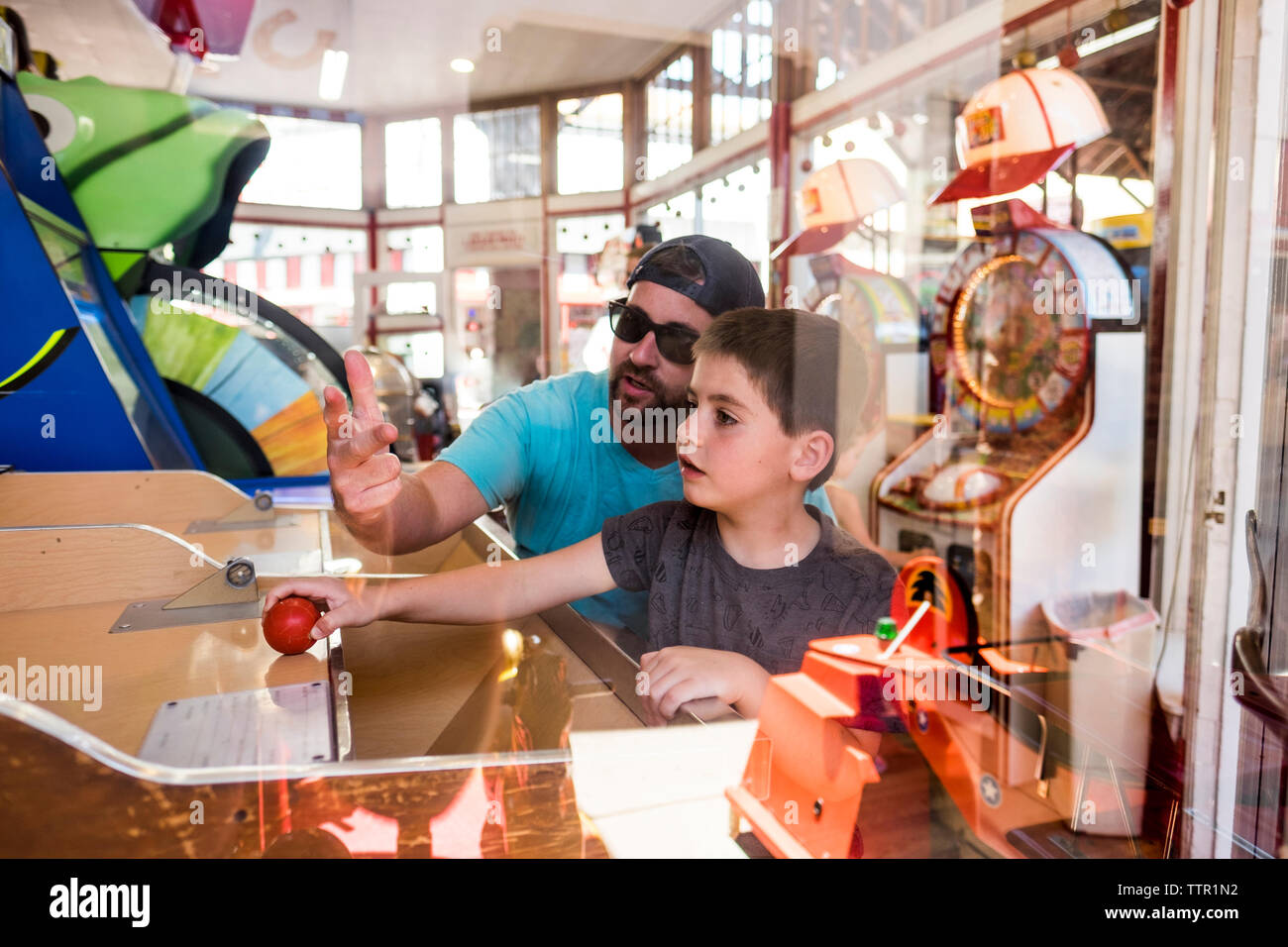 Father and son playing game at amusement arcade seen through window ...