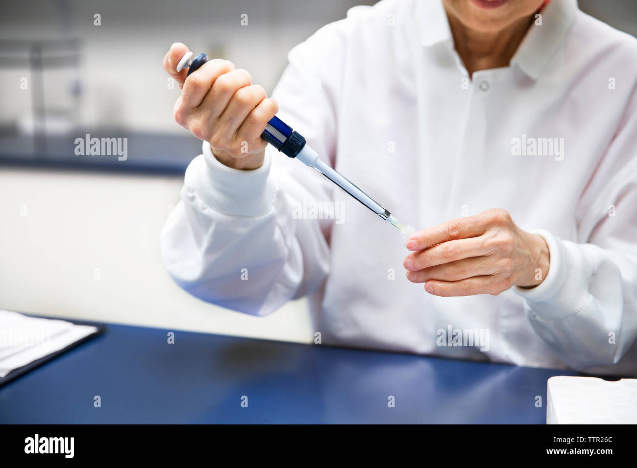 Senior female scientist pouring chemical through pipette in laboratory ...