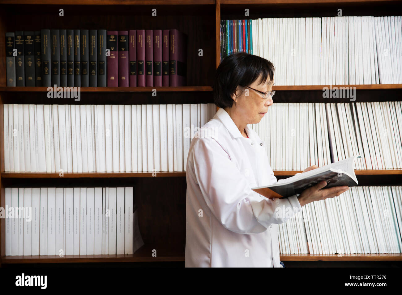 Senior female scientist reading book by shelves at laboratory Stock ...