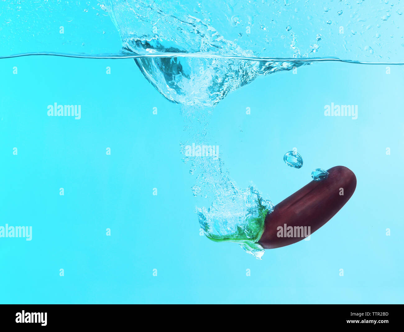 Eggplant falling into water on color background Stock Photo - Alamy