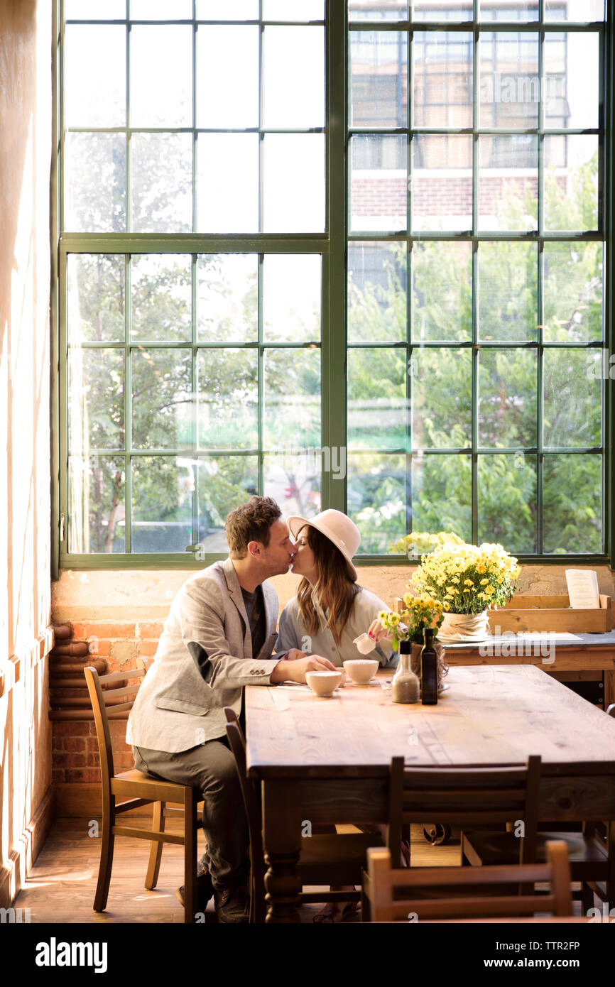 Couple kissing while sitting by table in restaurant Stock Photo - Alamy