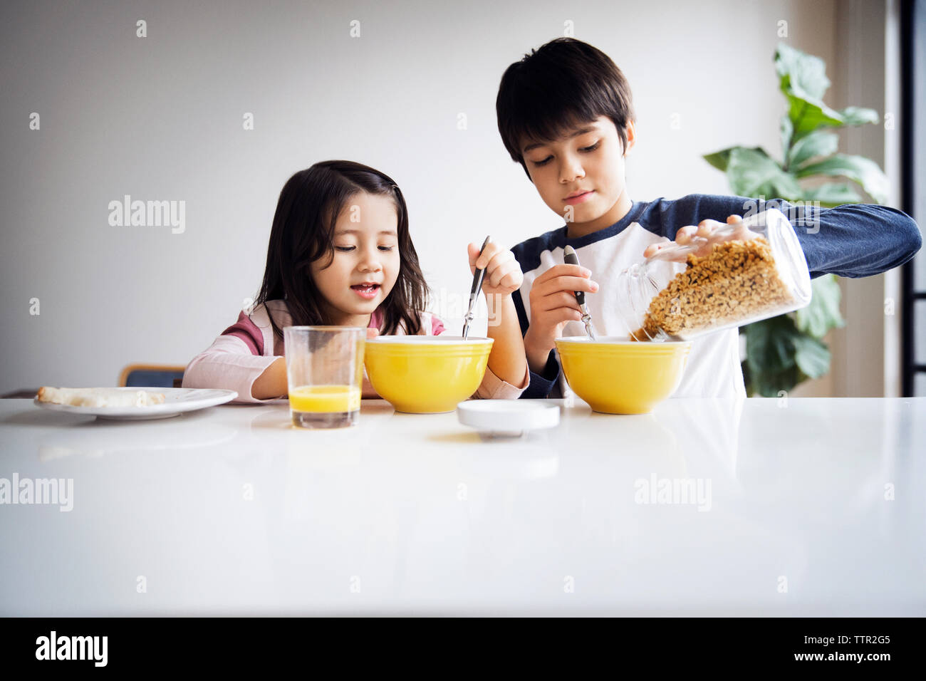 Happy siblings eating breakfast on table at home Stock Photo - Alamy