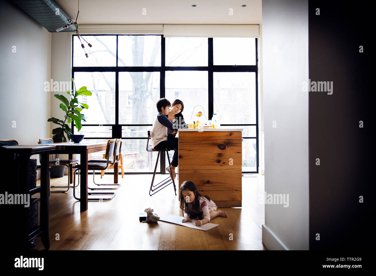 Mother assisting son in doing homework while sister studying on floor ...