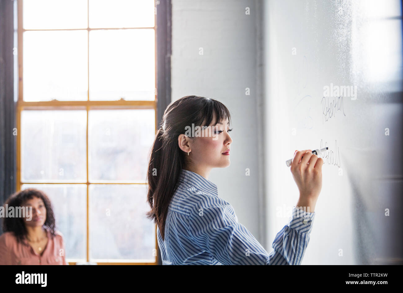 Side view of businesswoman writing on whiteboard in creative office ...
