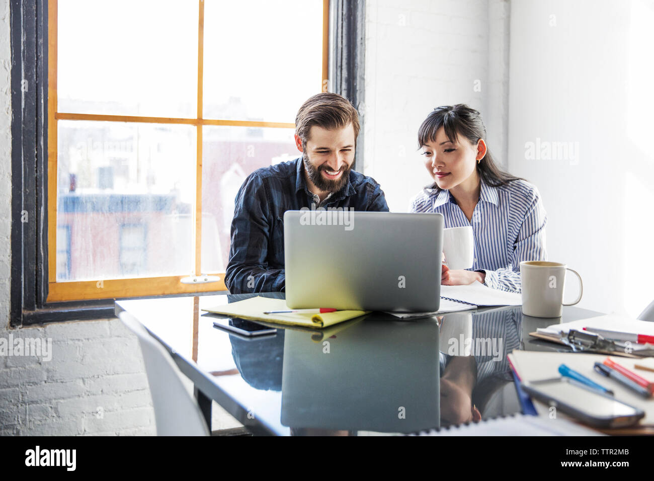 Smiling business people using laptop at creative office Stock Photo - Alamy