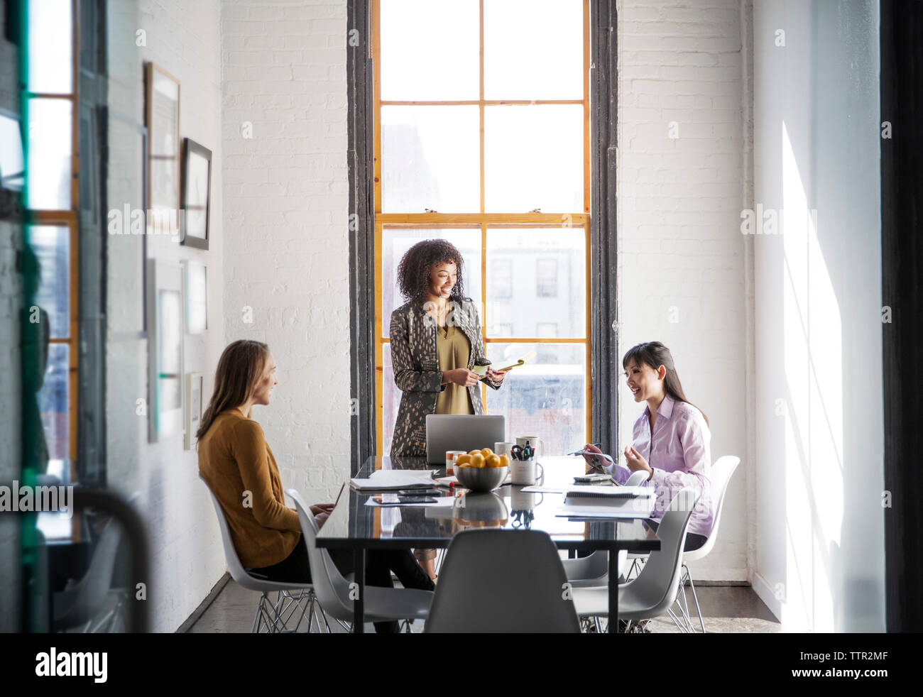 businesswomen discussing at table against window in creative office ...