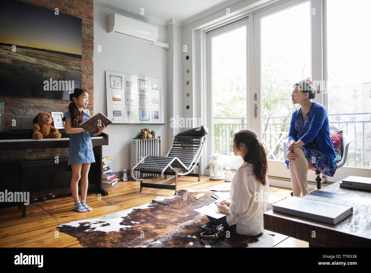 Girl holding book and explaining mother and sister at home Stock Photo ...