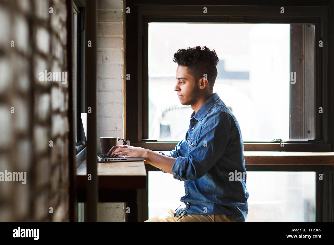 Side view of serious man using laptop while sitting by windows at cafe ...