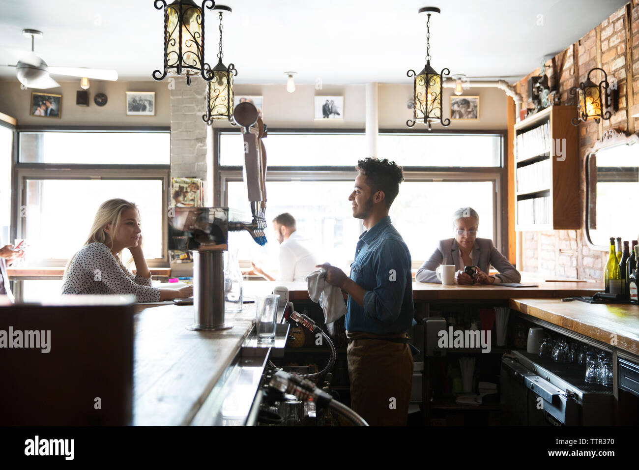 Smiling owner talking to customer while standing at bar counter in cafe ...