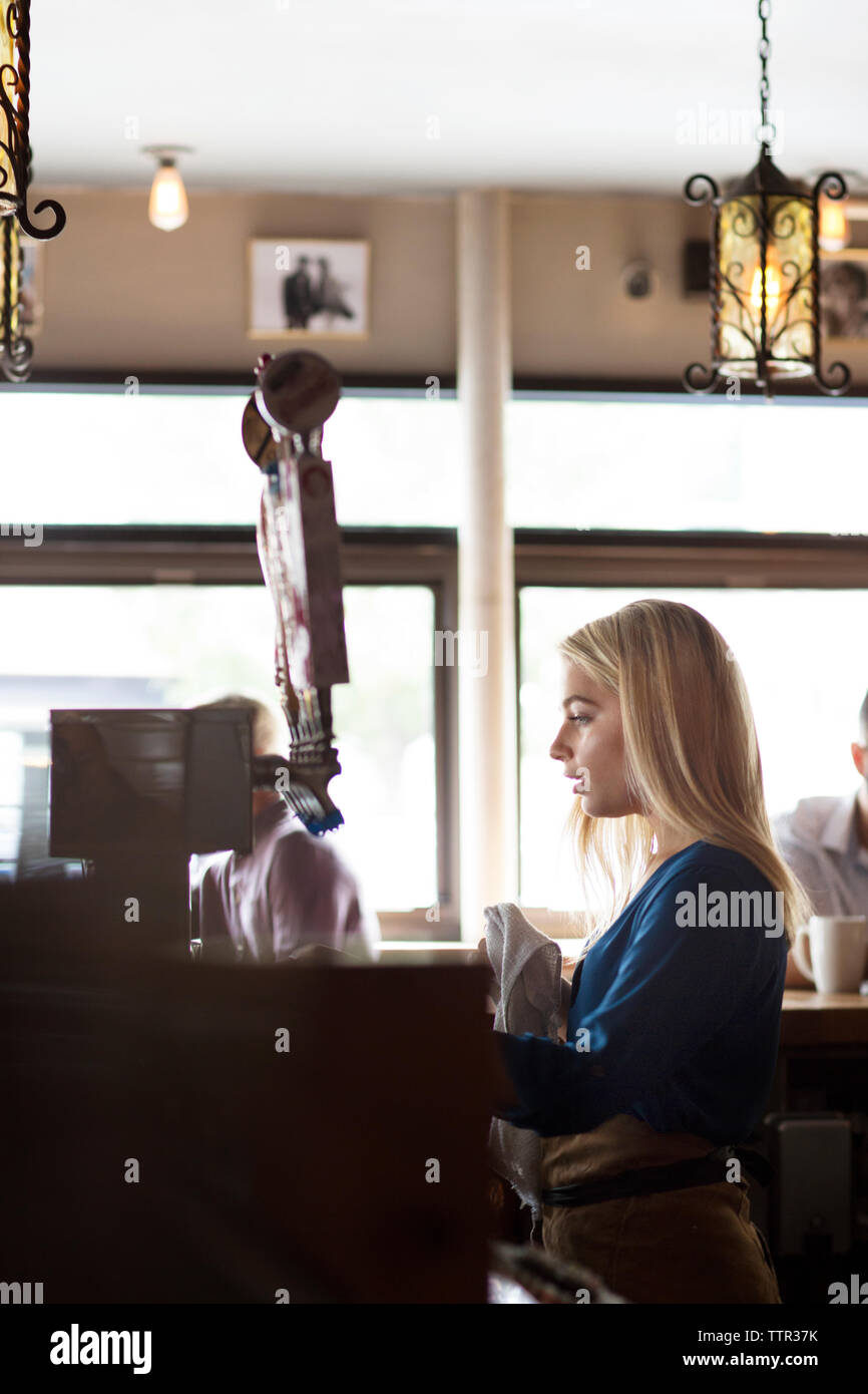 Side view of female standing at bar counter by customers in cafe Stock ...