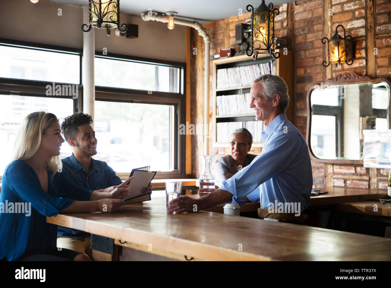 Male owner serving drinks while talking to customers at bar counter in ...