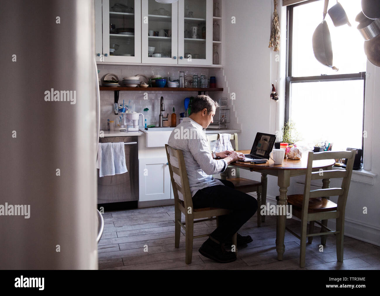 Side view of man using laptop computer while sitting at dining table in ...