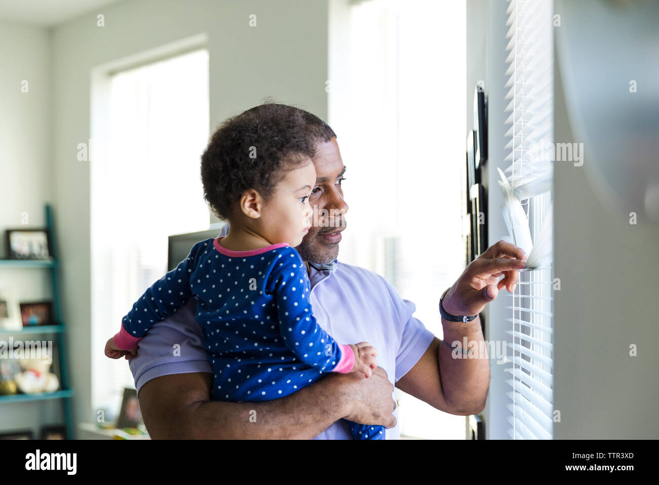 Father and daughter looking through window blinds at home Stock Photo ...